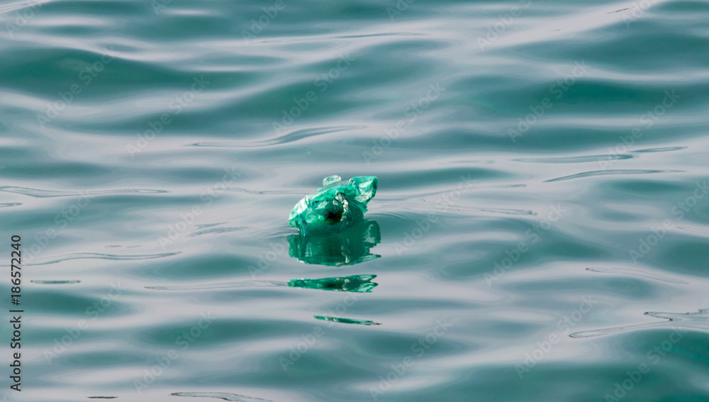 A green plastic bag floats on the surface of a turquoise sea. Plastic ...