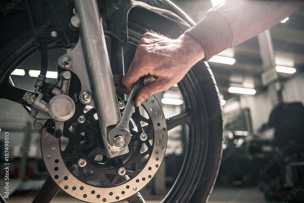 Close up of man's hand holding mounting wrench near the motorcycle's ...