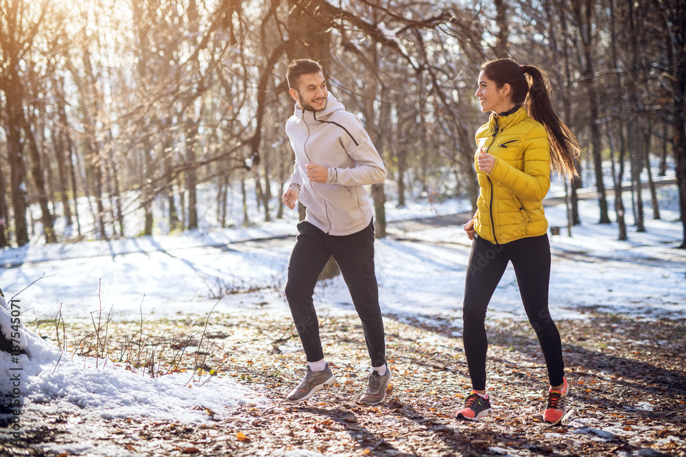 Side view of young happy charming smiling fitness sporty couple in winter sportswear jogging in ...