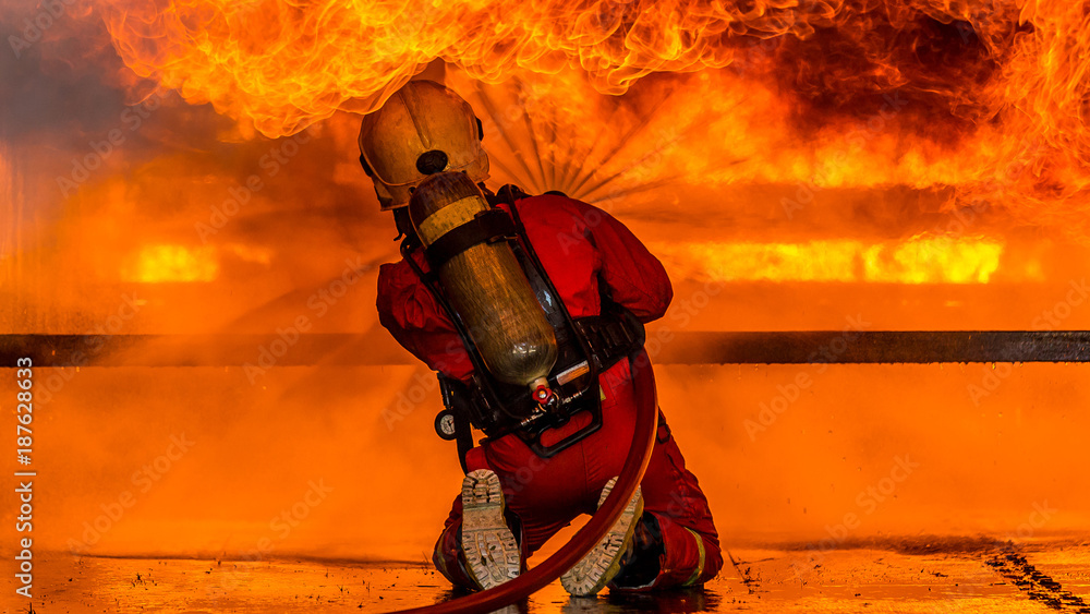Fireman in helmet and oxygen mask spraying water to fire surround with ...