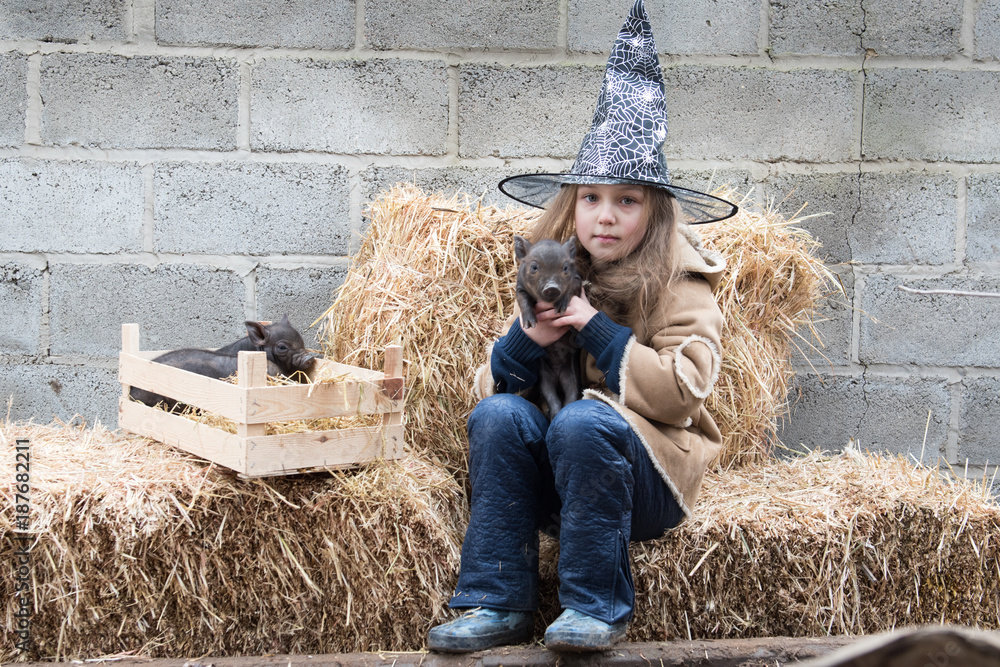 A happy girl in a witch's masked hat plays with newly born pigs. Winter ...