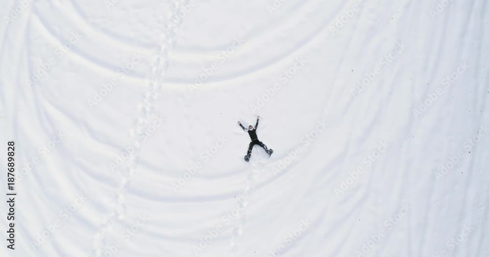 Overhead aerial top view over man lying doing snow angel with snowshoes ...