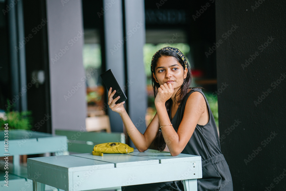 portrait of young woman sitting and resting her arms on a table at a ...