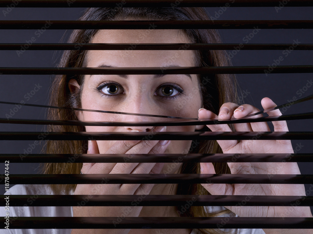 Teen behind a blind, surprised by what she sees. Stock Photo | Adobe Stock