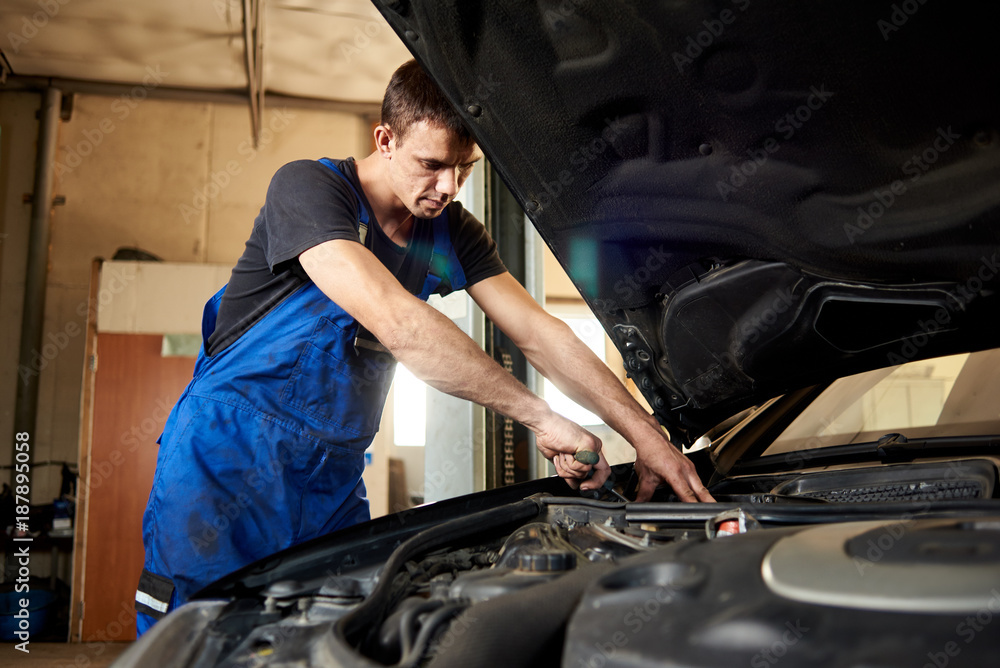 An auto mechanic in a dirty work uniform repairs a car in the garage ...