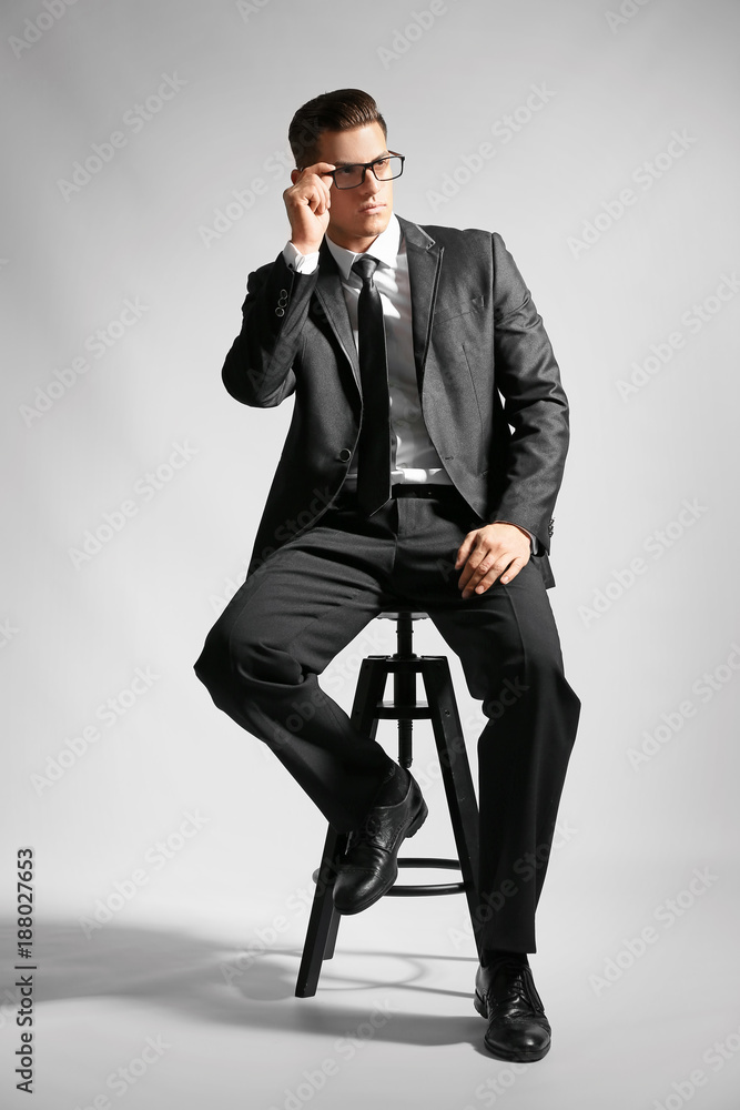Handsome man in elegant suit sitting on chair against light background ...