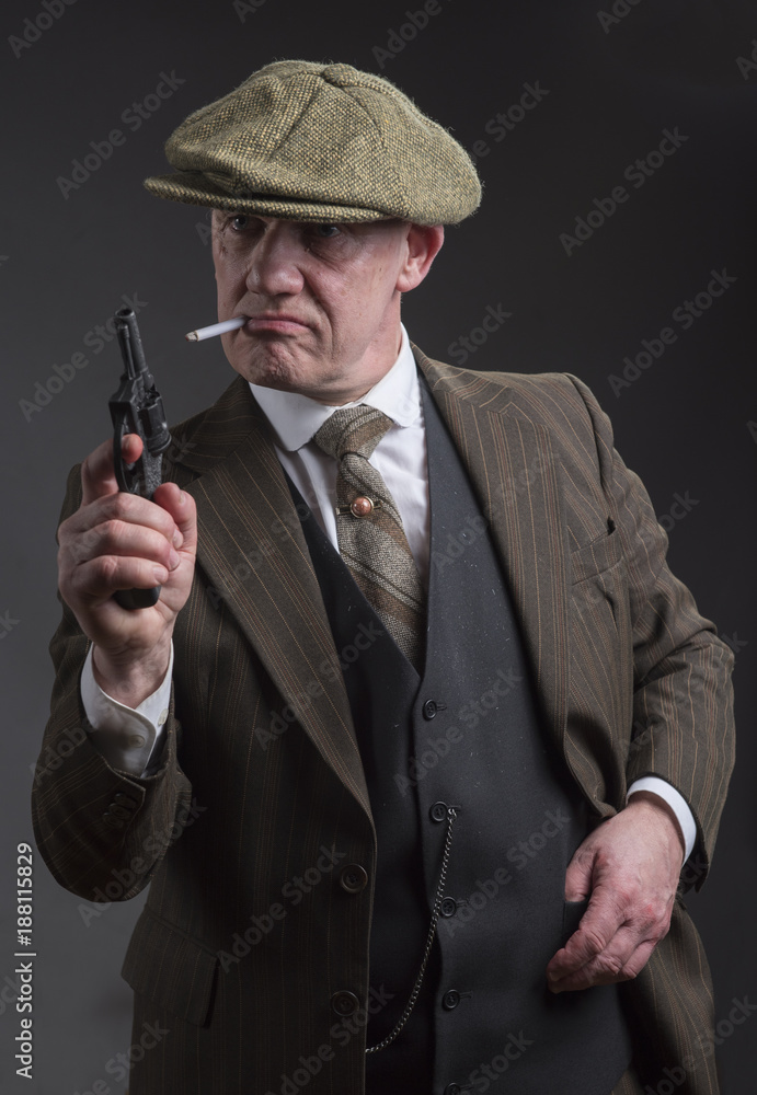 Mature man in Victorian gangster outfit holding a hand gun and smoking ...