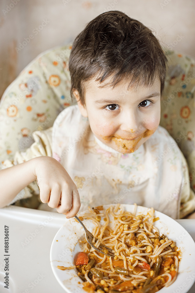 Child eating spaghetti with vegetables. Kid having fun eating. Brown ...
