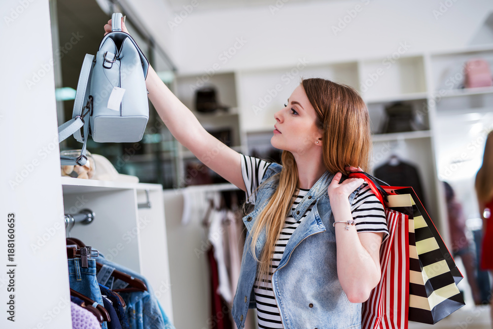 Young female shopper with shopping bags choosing the handbag matching ...