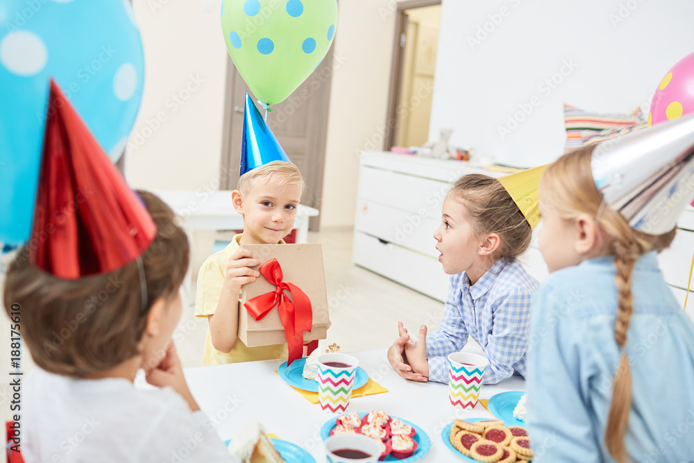 Cute boy opening box with present during birthday party among his ...