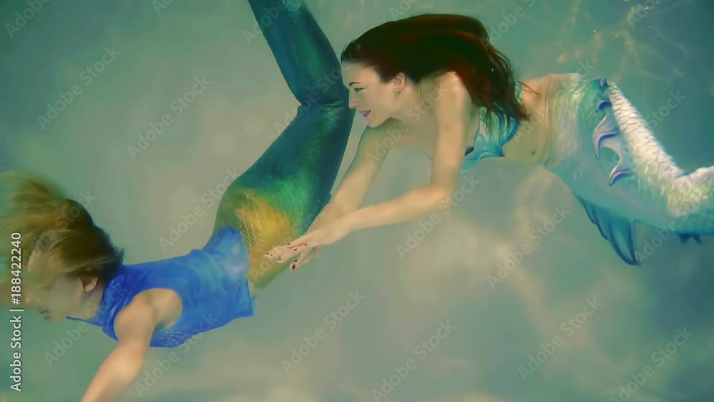 two actresses is wearing fake mermaids costumes and floating under ...