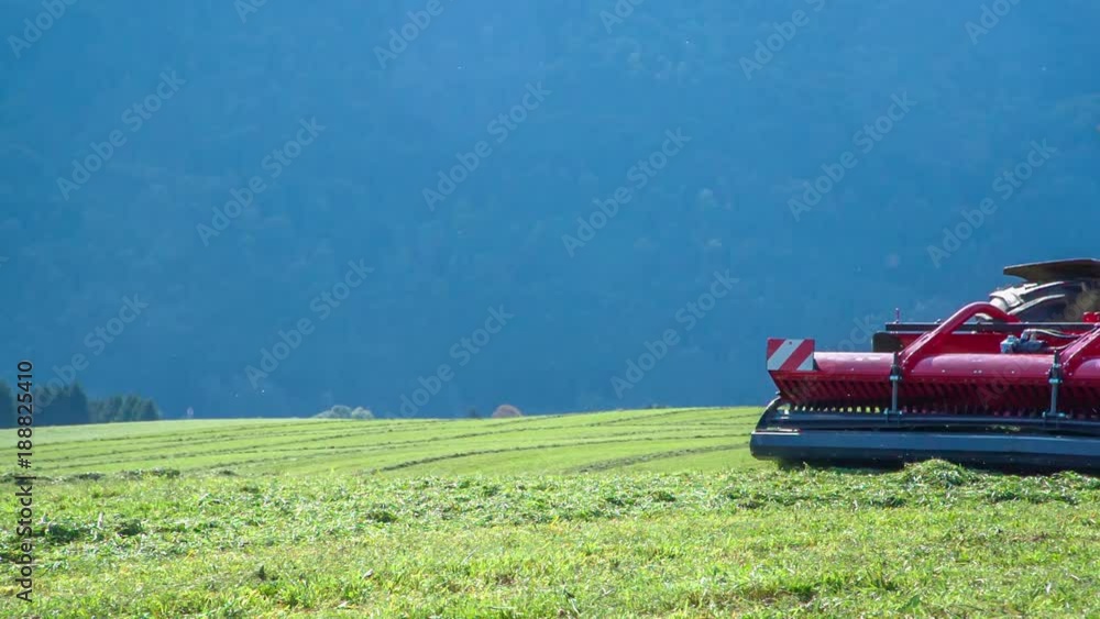 A big tractor is cutting grass with the machinery which is in front of ...