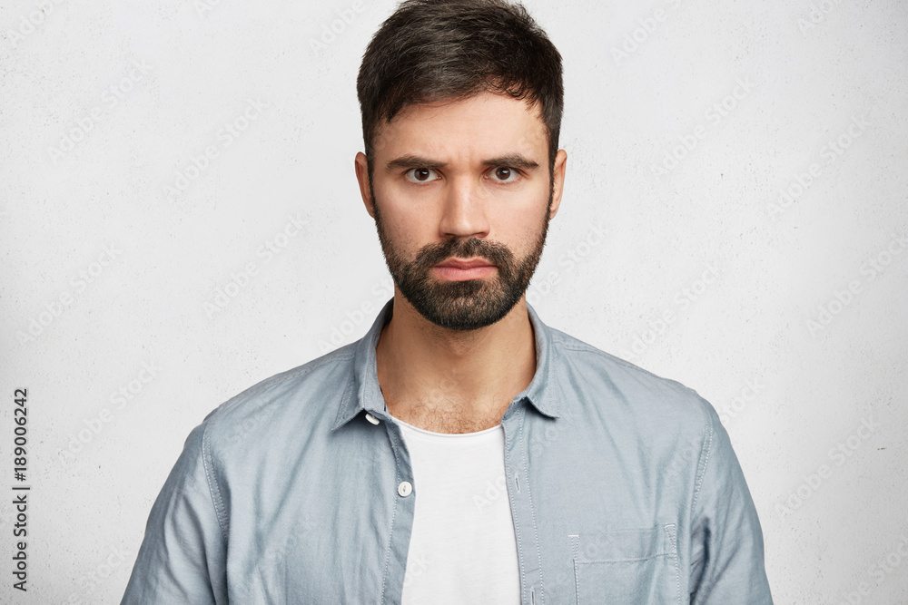 Studio shot of serious strict male with dark beard and mustache, looks ...