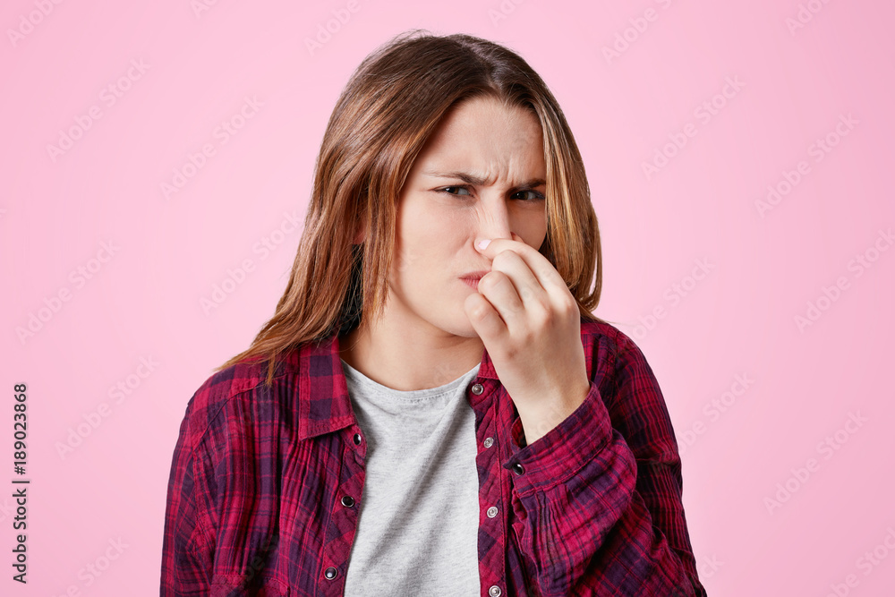 Foto de Displeased female model plugs nose as smells unpleasant scent ...