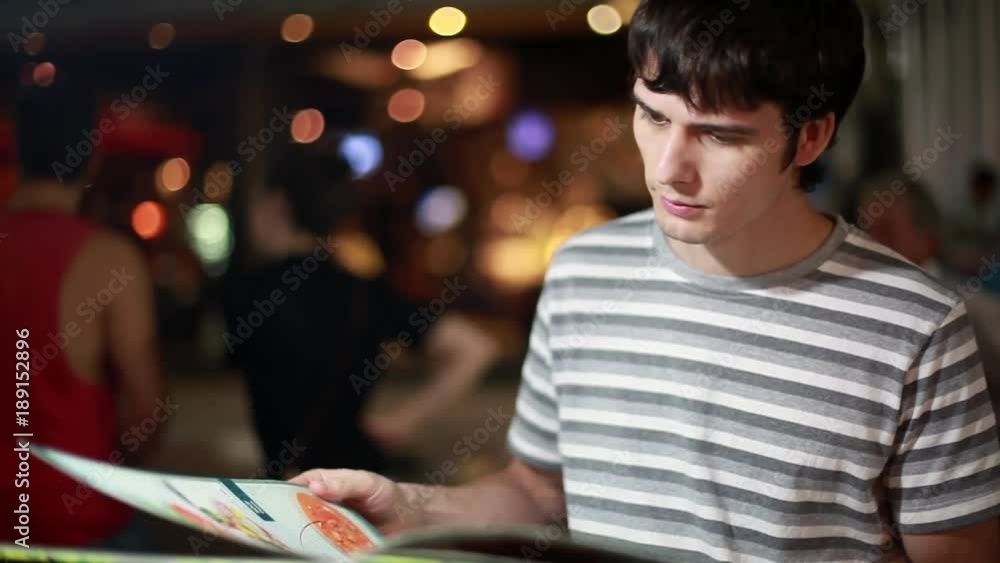 Handsome young man reading menu in an outdoor cafe on blurred bokeh ...
