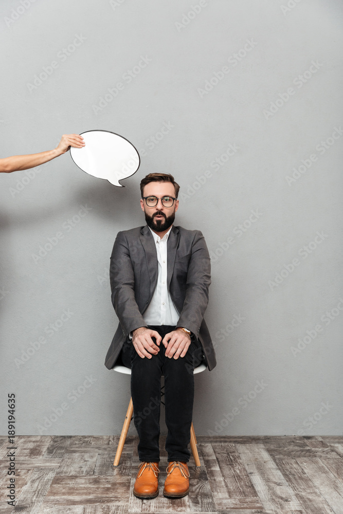 Full-length portrait of young man sitting on chair putting hands down ...