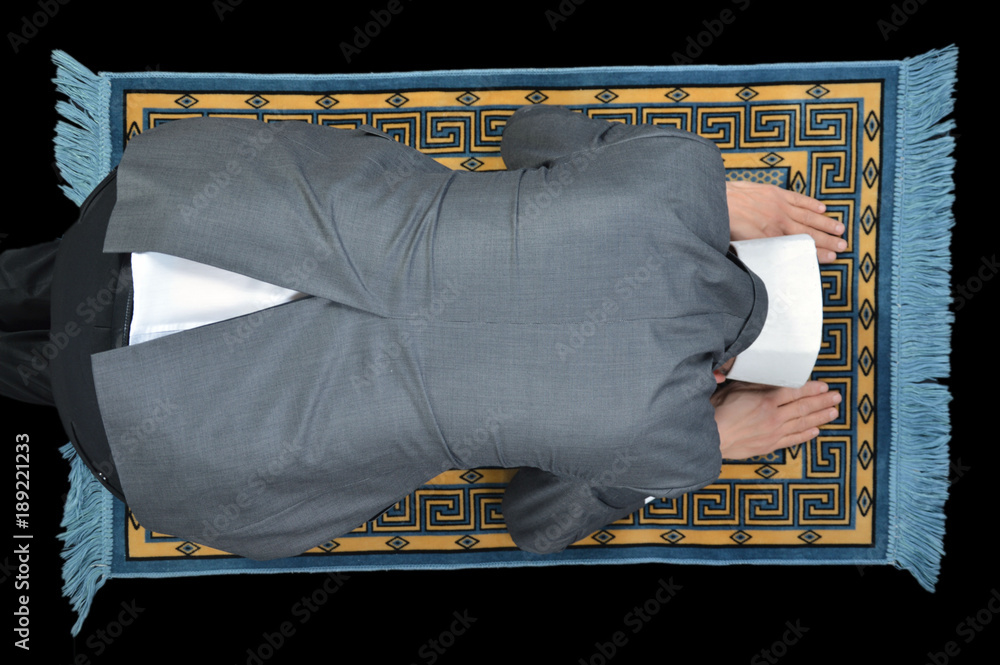 Overhead view of man praying on prayer mat against black background ...