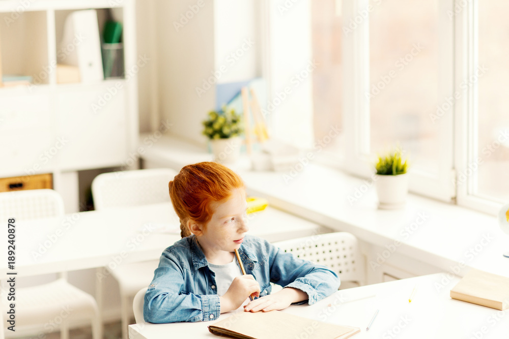 Thoughtful little girl sitting by desk, looking through window of ...