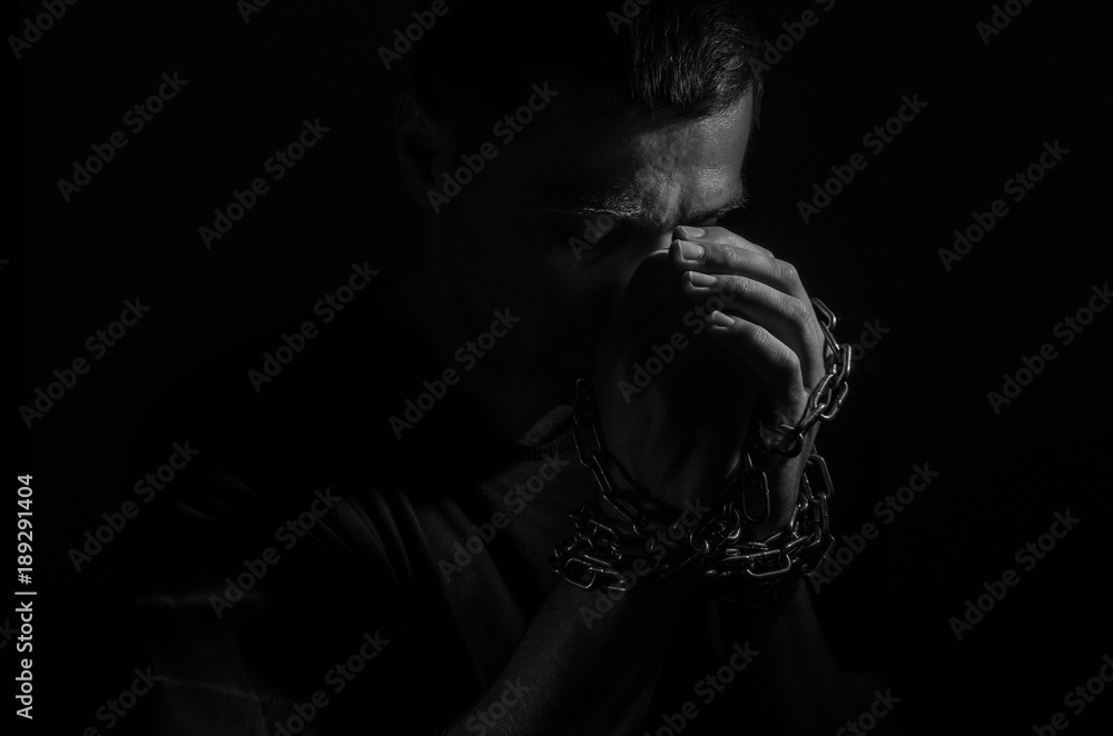 Repented man prisoner with his hands shackled in chains on a dark ...