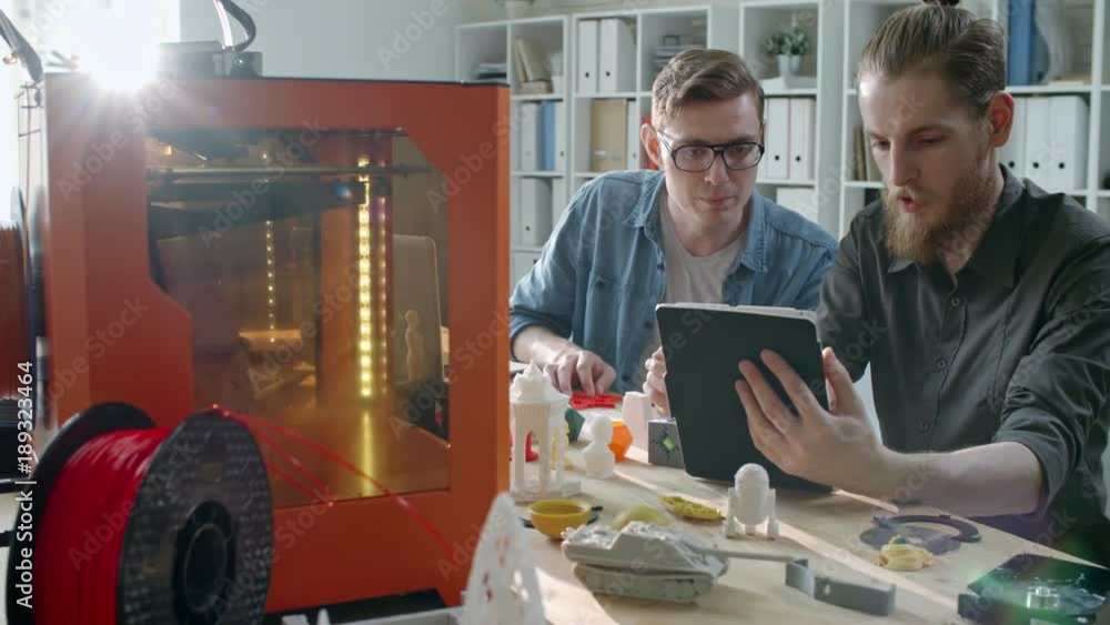 Two young men controlling 3D printing process via digital tablet while ...