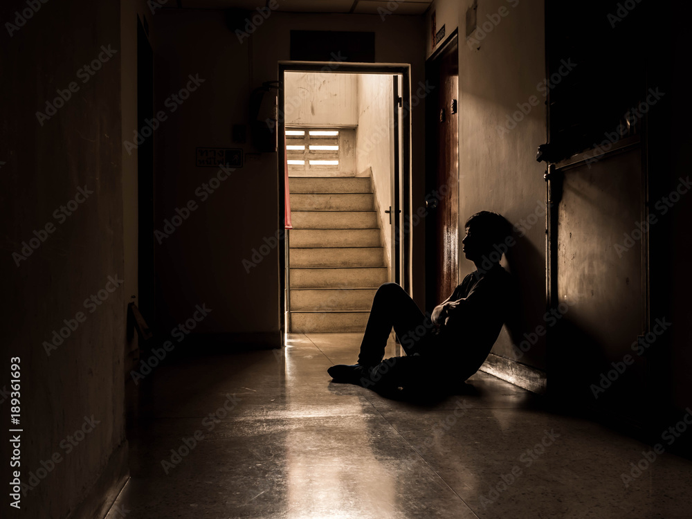 Silhouette of a sad young man sitting in the dark leaning against the ...