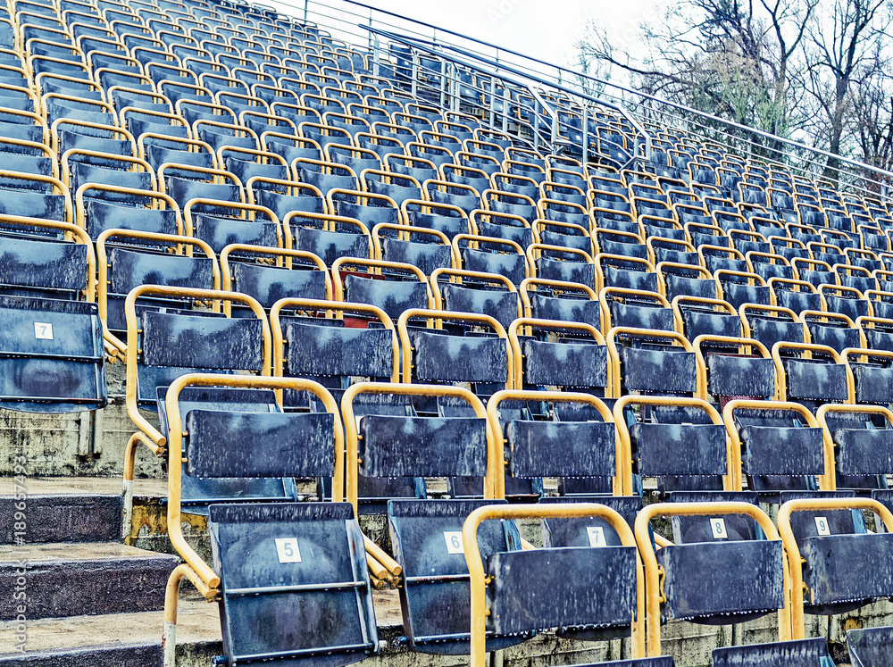 Folding seats of a street amphitheater are under heavy rain. On each ...