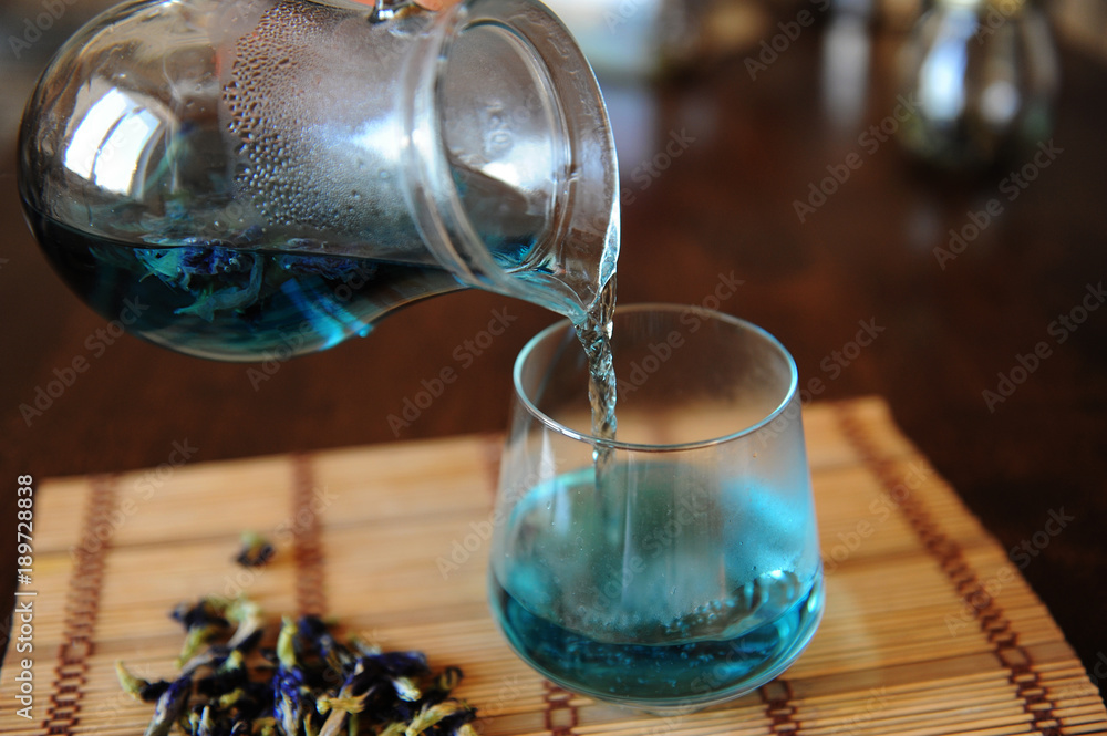 Blue Thai tea anchan is poured from jug into glass. Placer of dried ...
