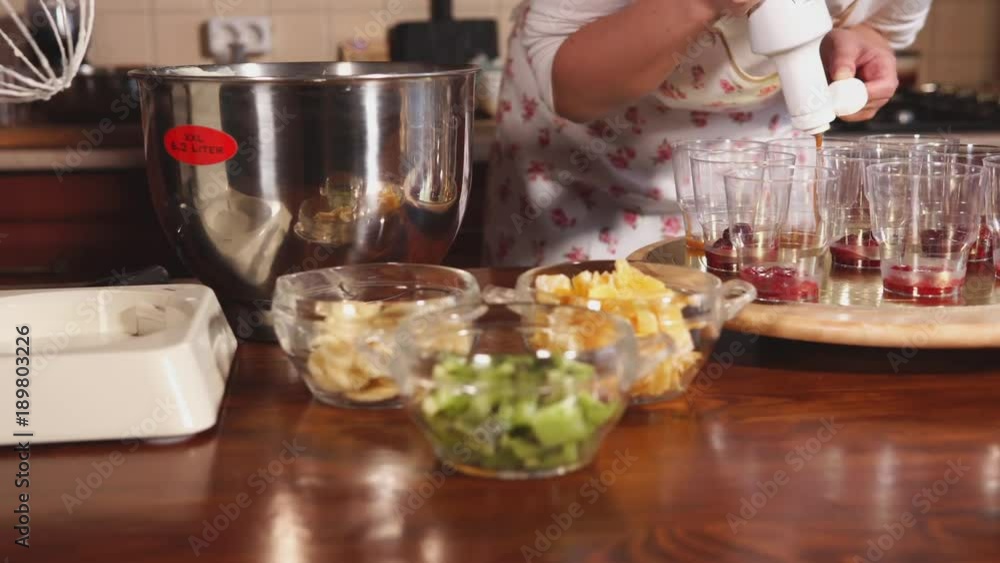 Female cook is making new desserts in her kitchen. She is filling cups ...