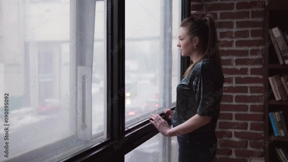 Vidéo Stock Sad woman goes to the window and looks at the city street ...