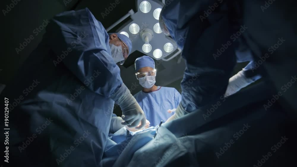 Zoom out shot of team of surgical care practitioners stitching incision ...