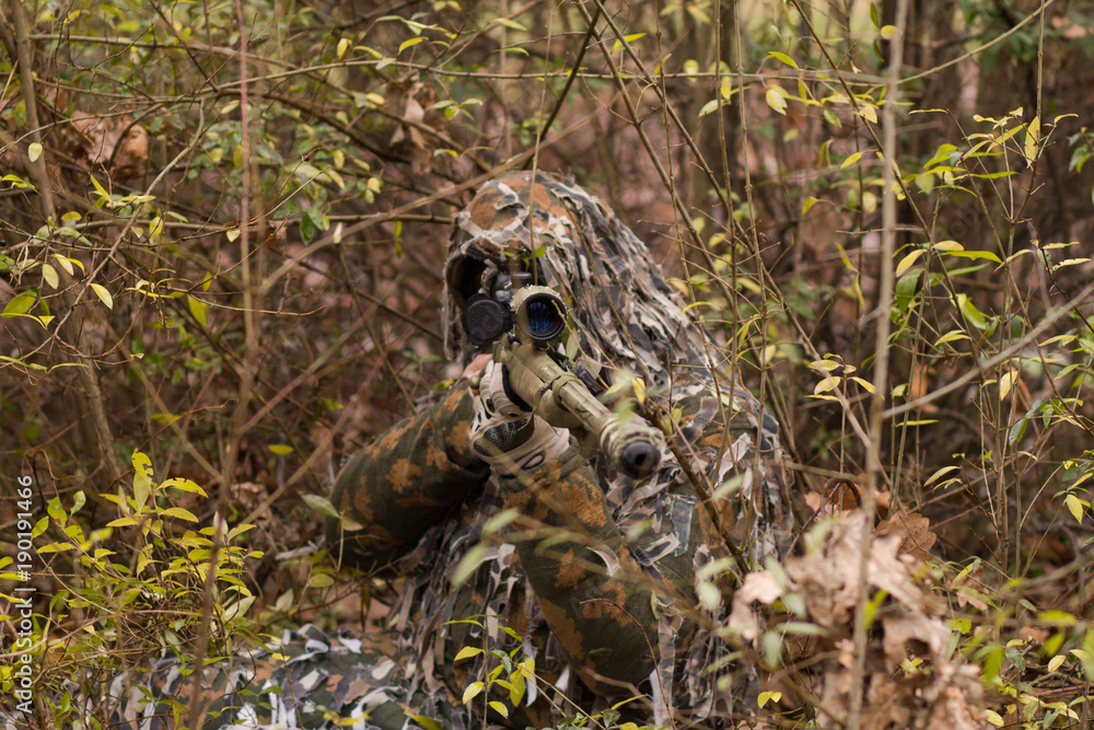 Hunter or soldier hiding in bushes, autumn forest background. Sniper ...