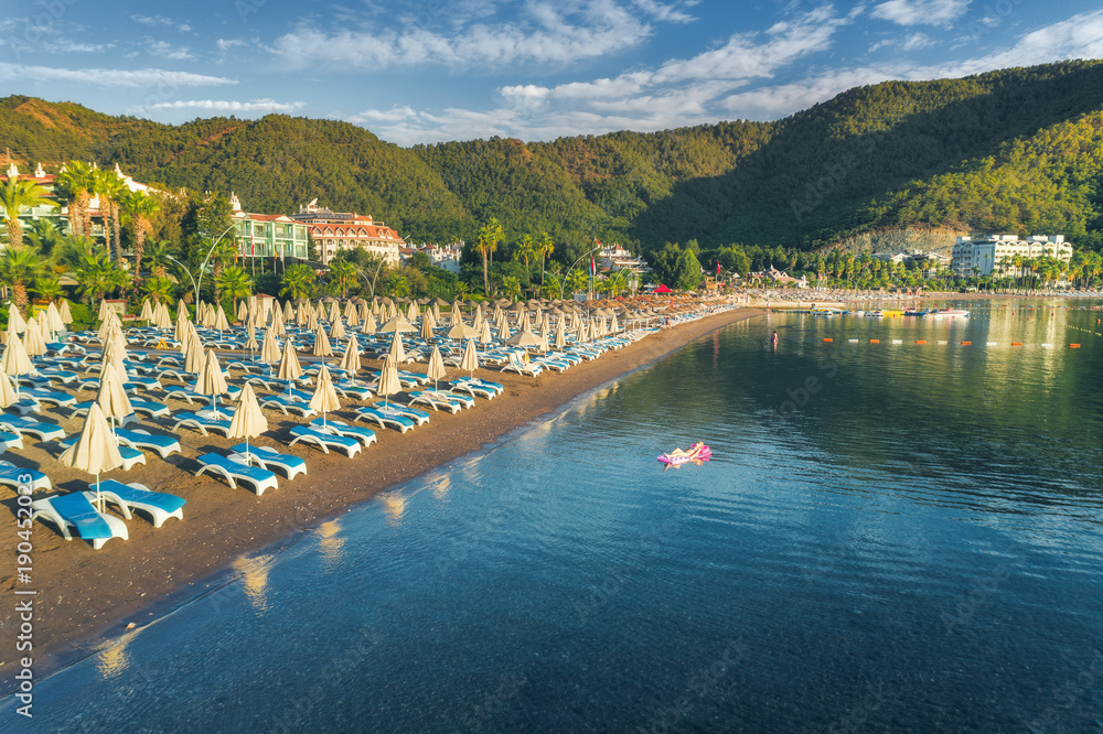 Aerial view of beautiful beach with chaise-lounges and swimming woman ...