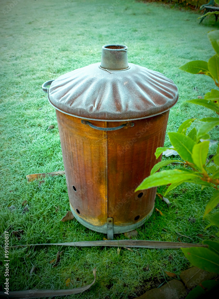 a rusty garden fire bin with a coating of white frost on it, green ...