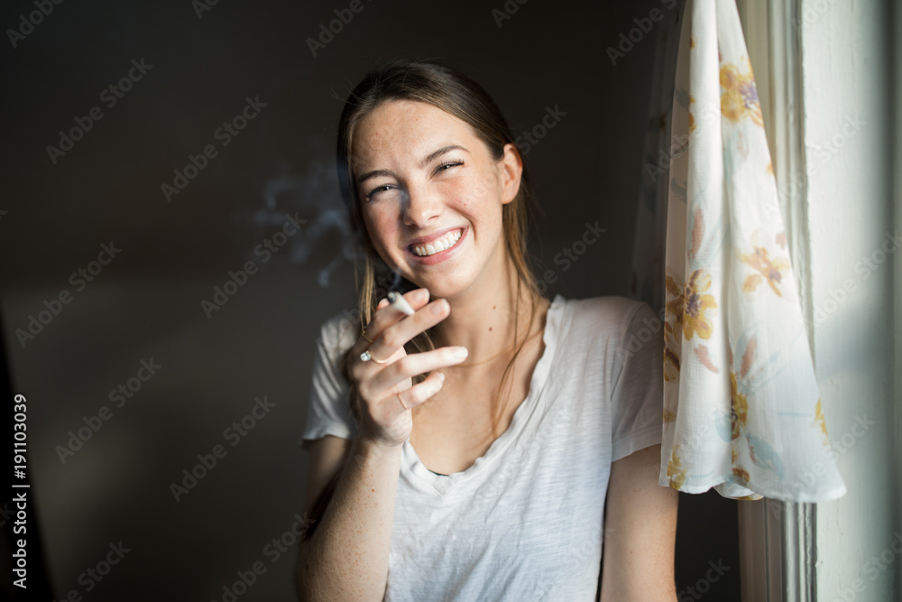 Portrait of a smiling woman smoking a joint while standing indoors ...