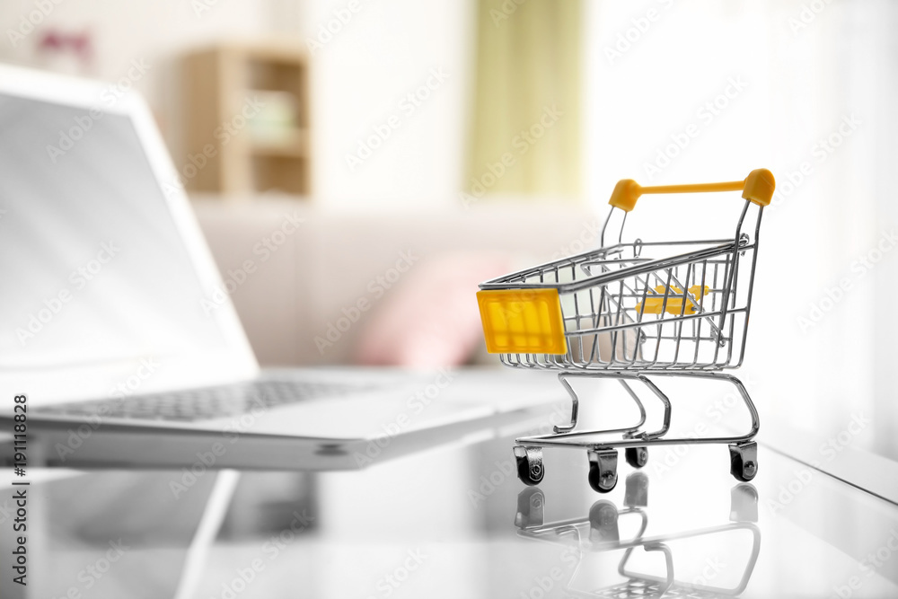 Laptop and small shopping cart on table. Internet shopping concept ...