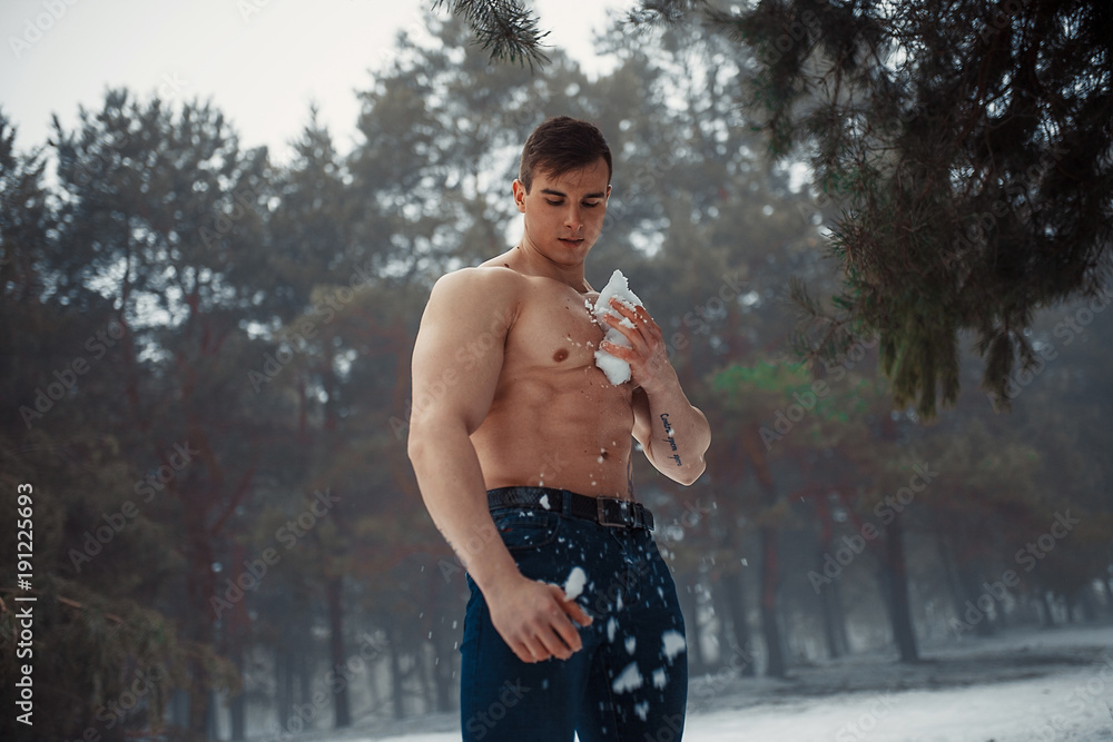 Young bodybuilder with bare torso wipes his body by snow in forest in ...