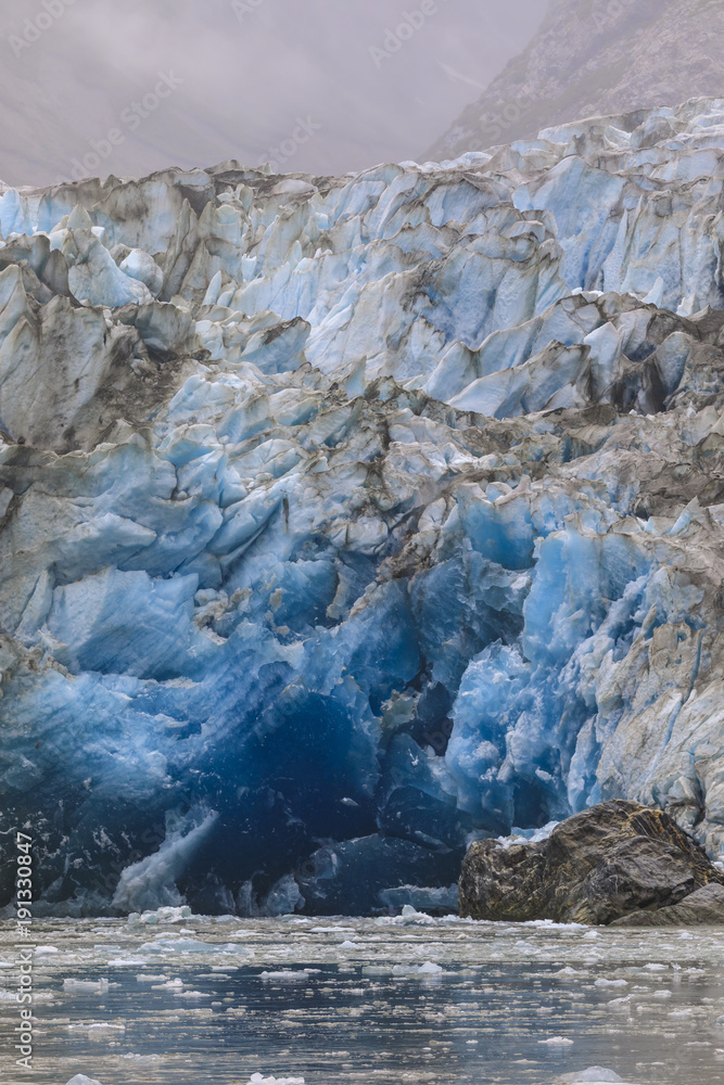 Blue ice face and floating ice, Sawyer Glacier and mountains, misty ...