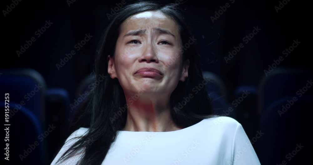 A beautiful, young asian woman at the movie theatre cries ...
