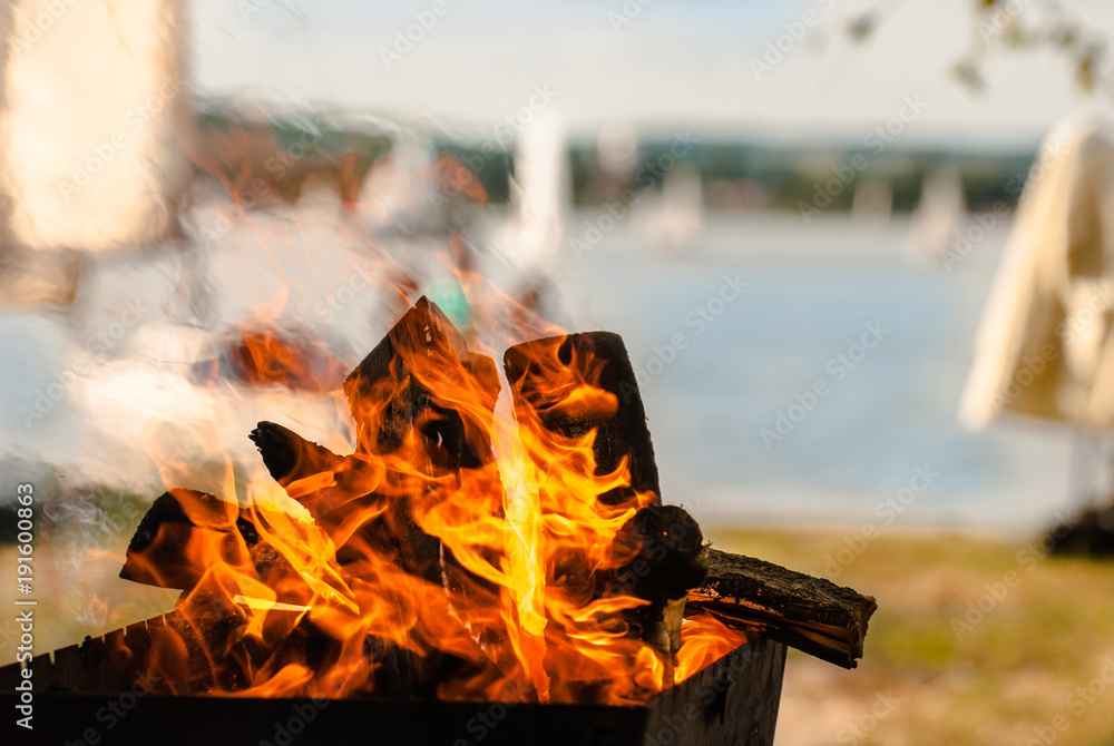 Inviting bonfire on the beach of the reservoir with yachts, people ...