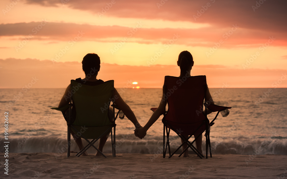 Couple relaxing on the beach watching the sunset holding hands. Stock ...