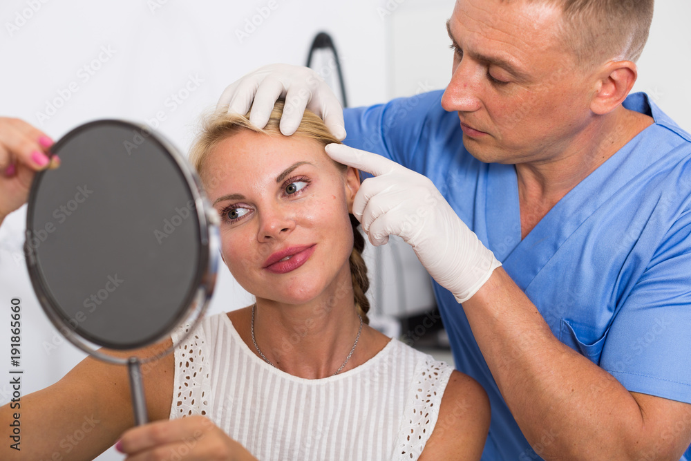 Specialist is analysing skin of female patient with using mirror before ...