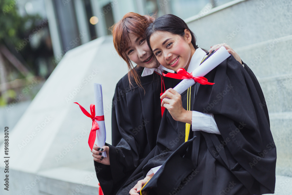 Portrait of Two happy graduated young girls in graduation gowns holding ...