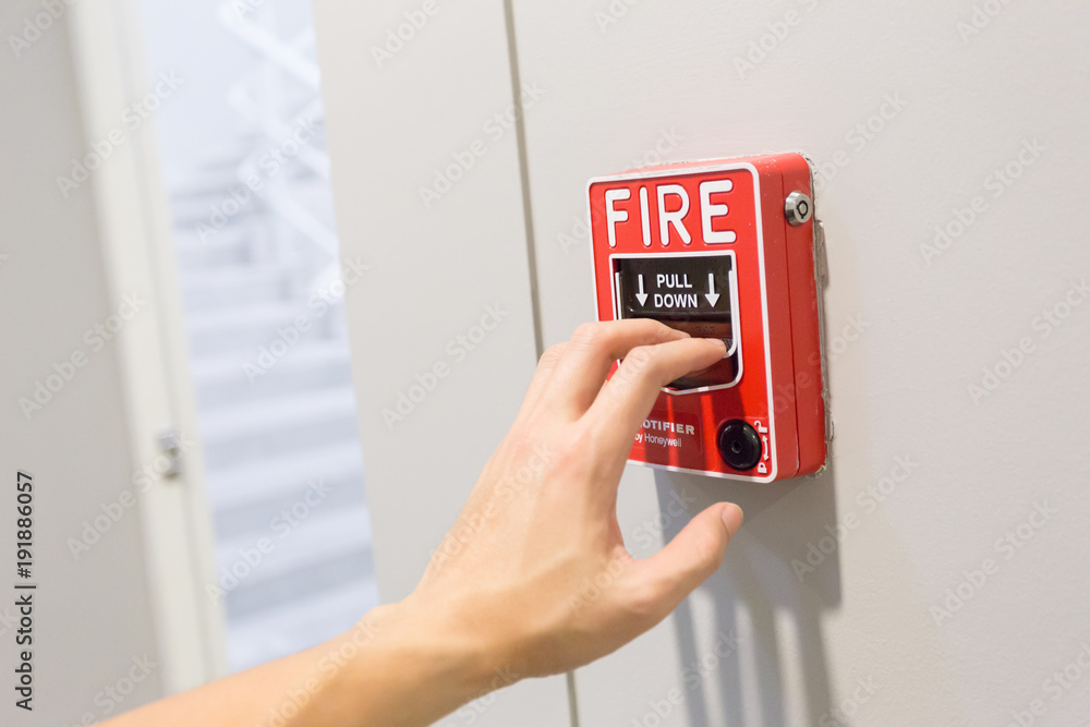The hand of man is pulling fire alarm on the wall next to the emergency ...