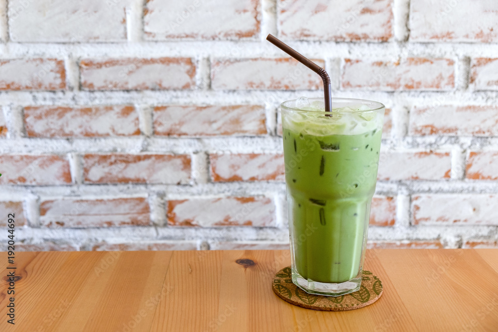 A glass of iced green tea with milk on wooden table with white brick ...