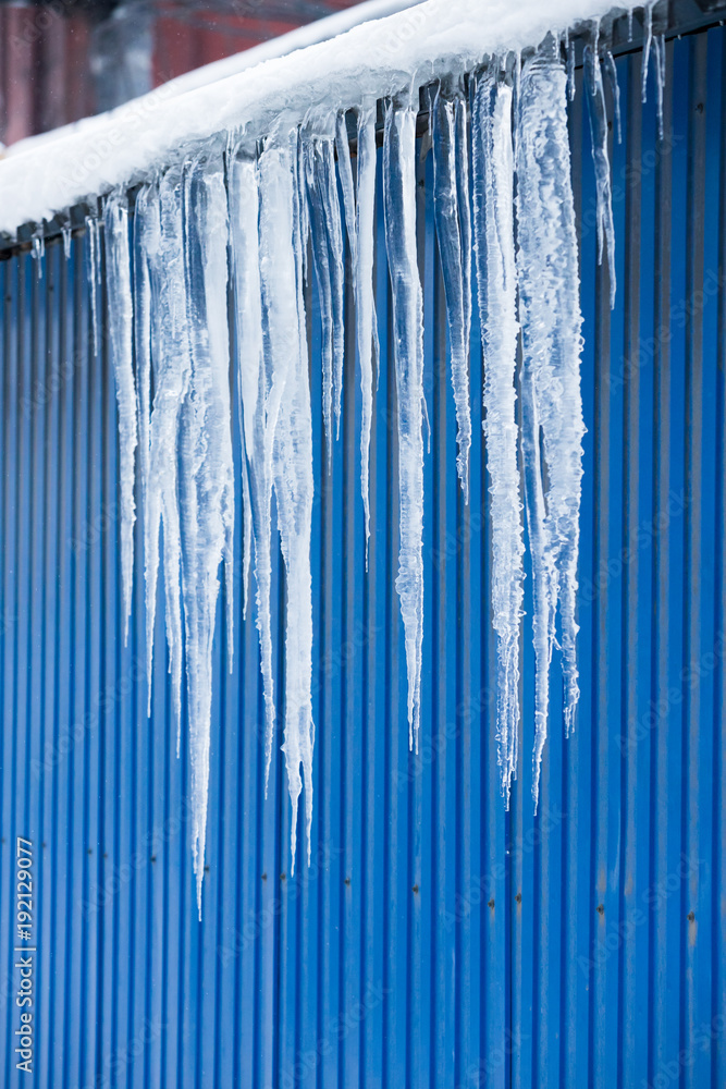 Roof of metal building with blue walls covered with sharp icicles/ Ice ...