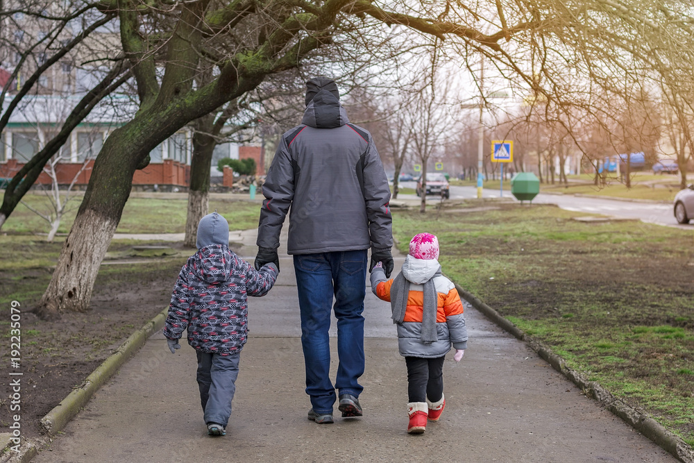 Father walking alone the street with two children, holds their hands ...