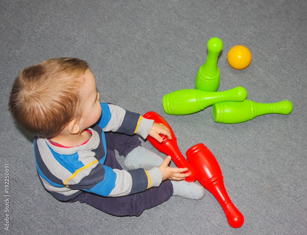 Baby and bowling. A little boy is sitting on the floor with skittles ...