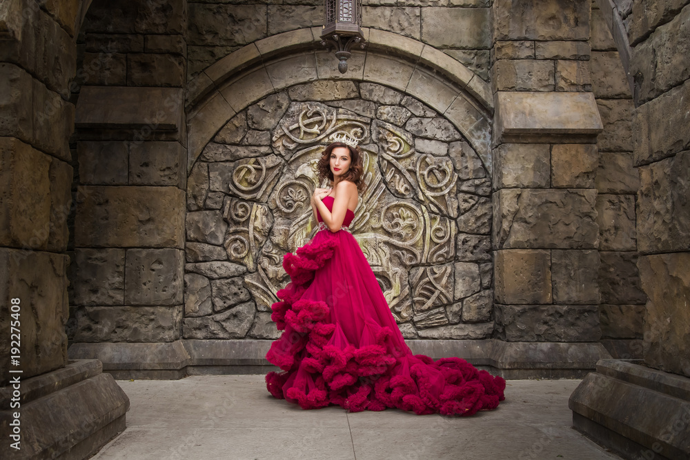 A beautiful woman, a queen in a red luxurious dress, stands on the ...