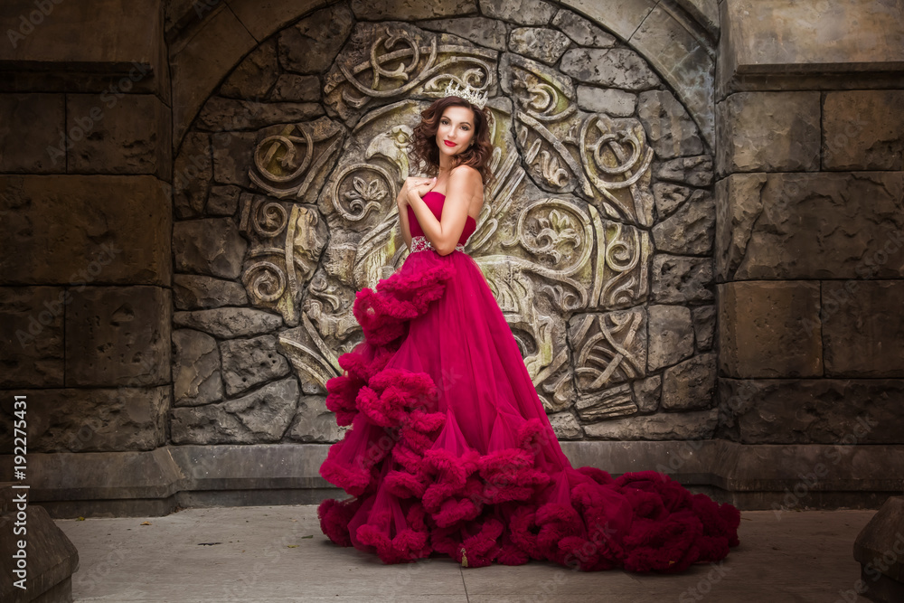 A beautiful woman, a queen in a red luxurious dress, stands on the ...