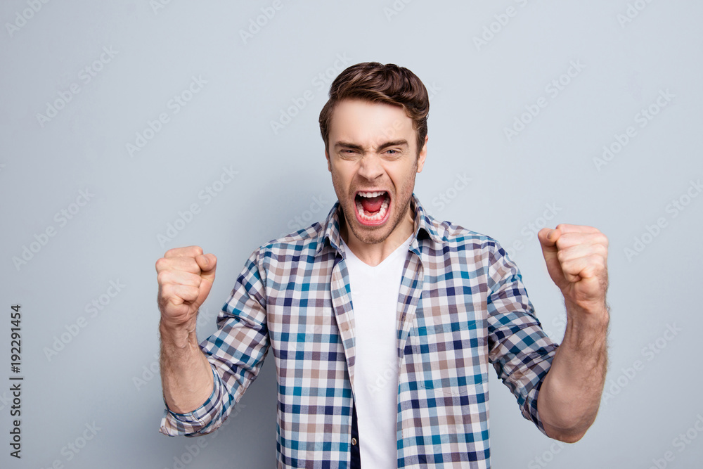 Aggressive man in checkered shirt with raised fists and open mouth is ...